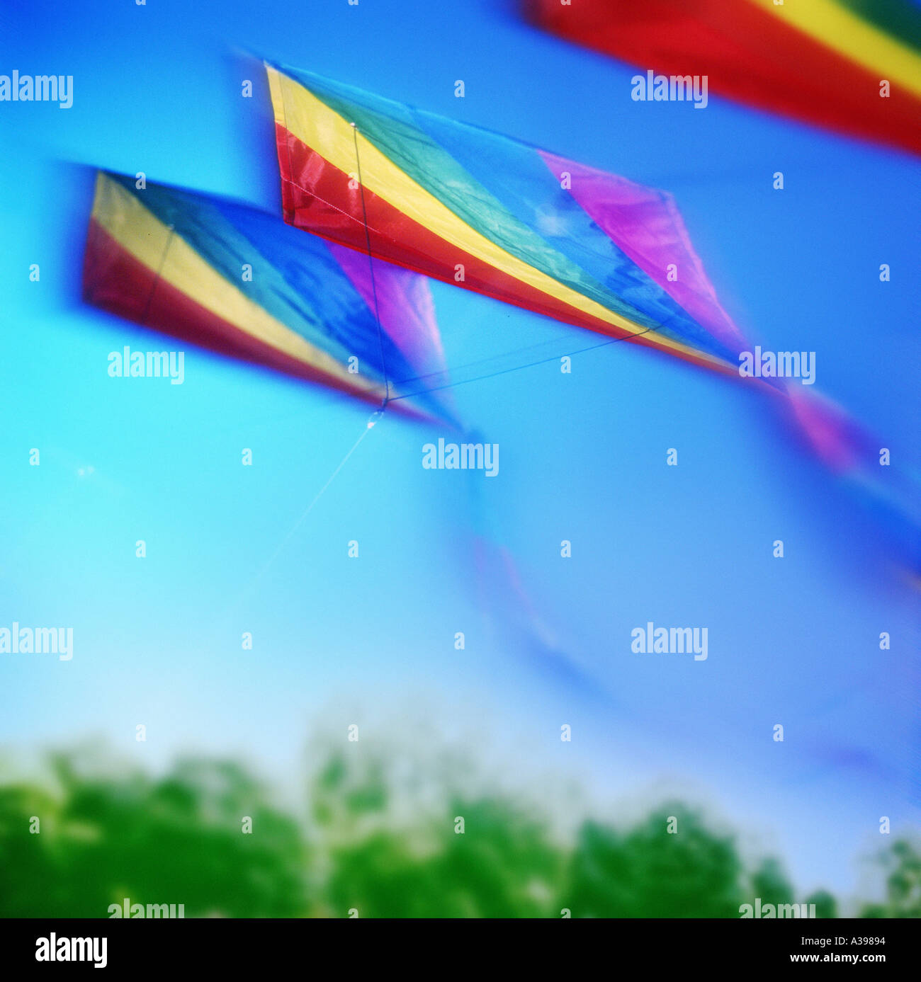 Three kites floating over some trees in a blue sky Stock Photo - Alamy