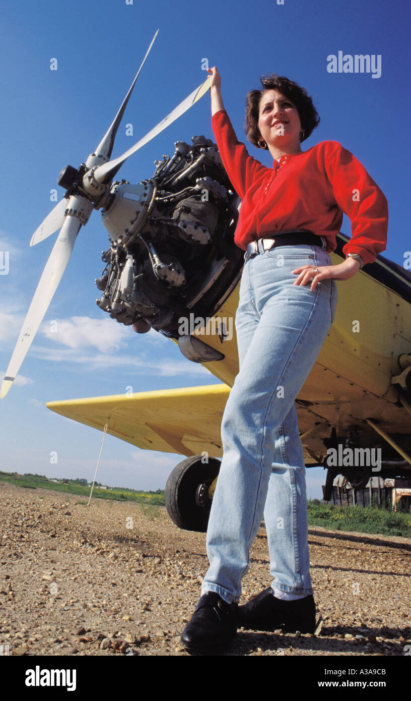 A confident young female pilot wearing jeans and a red blouse stands ...