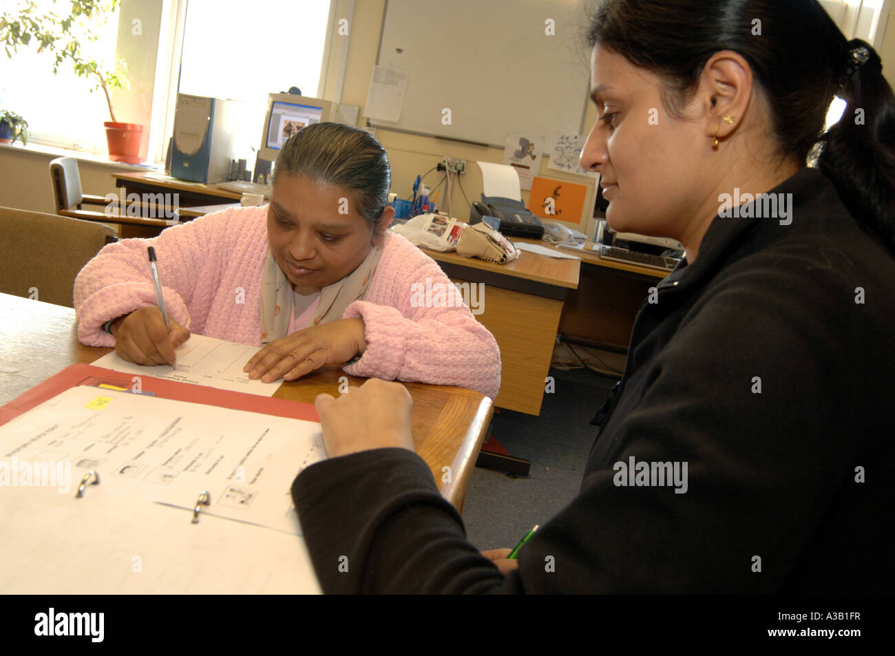 A woman with learning disabilities fill in a form with her carer ...
