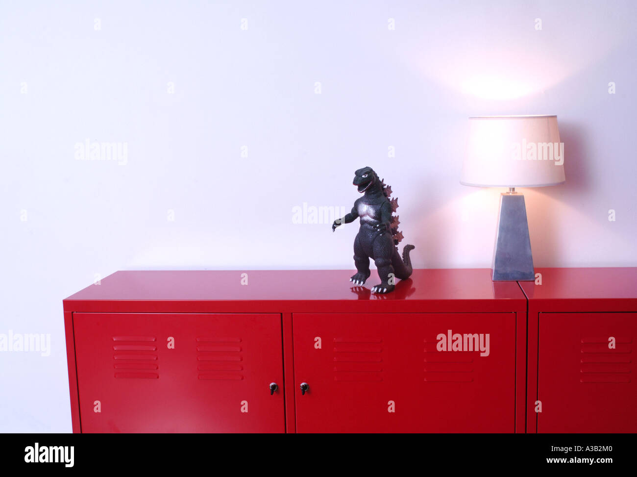 plastic Godzilla toy on red cabinet with lit lamp and white wall Stock ...