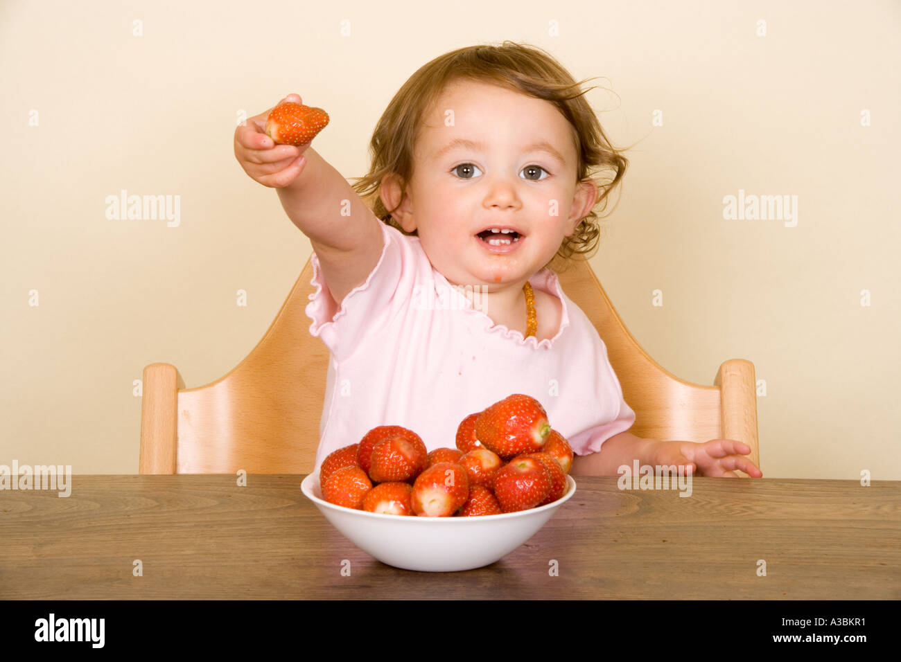Baby eating strawberries in high chair Stock Photo - Alamy