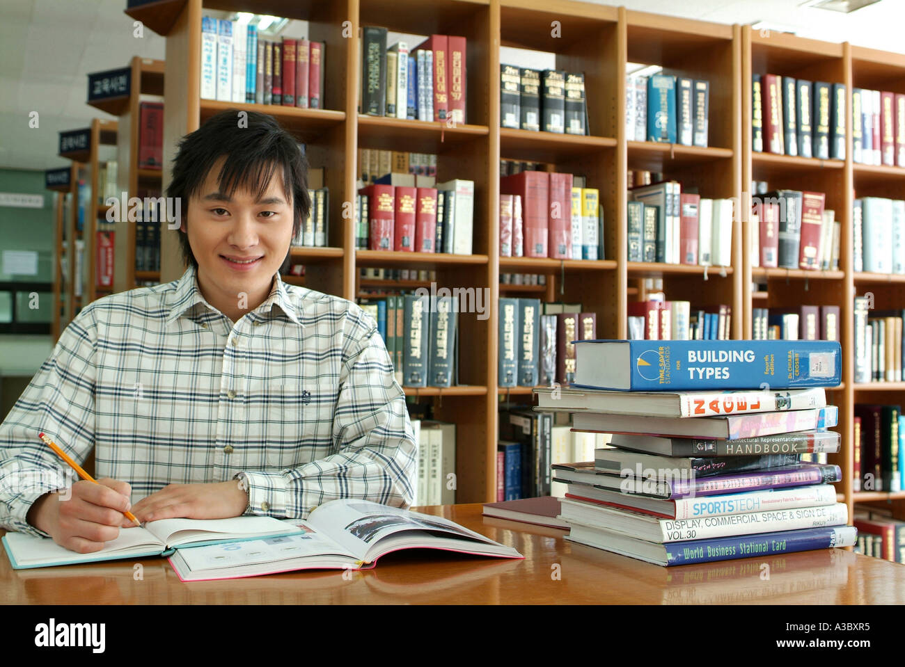 a man studying in the library and there are many books on the desk ...