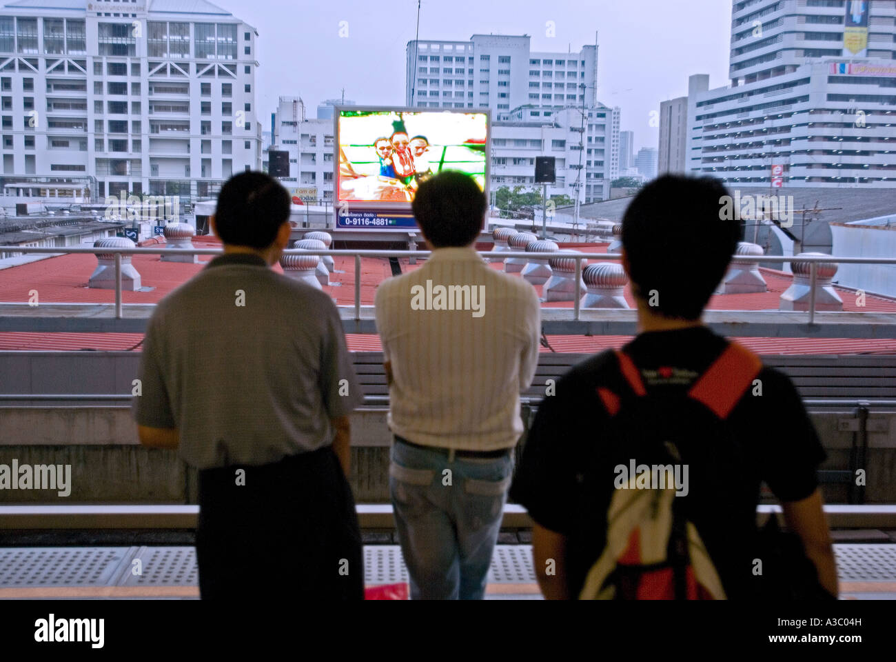 Three Skytrain commuters watching television on a huge monitor on the ...