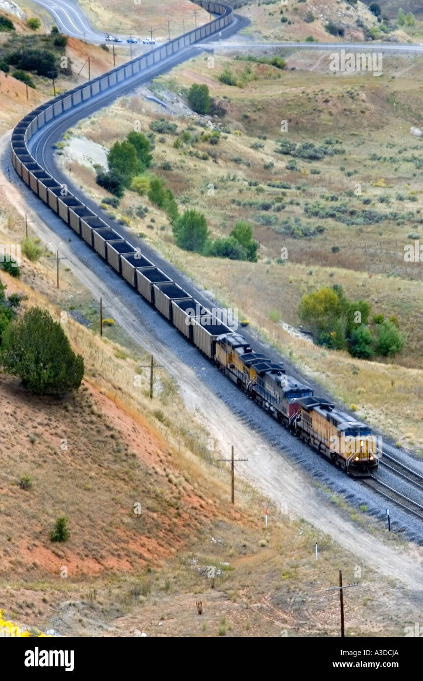 Loaded coal train stretches back across a highway crossing where cars ...