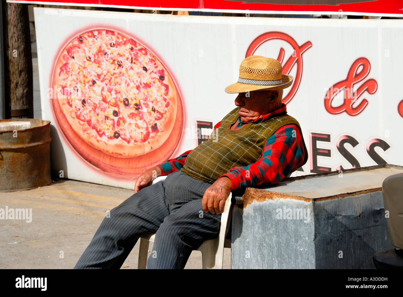Old man with a hat rests at a pizza sign in the old town of Famagusta ...