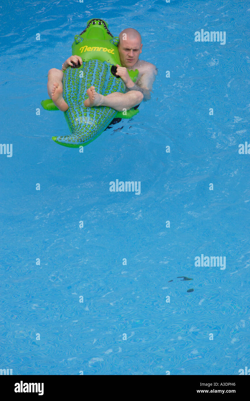 Man swimming in pool while holding onto crocodile shaped water float ...