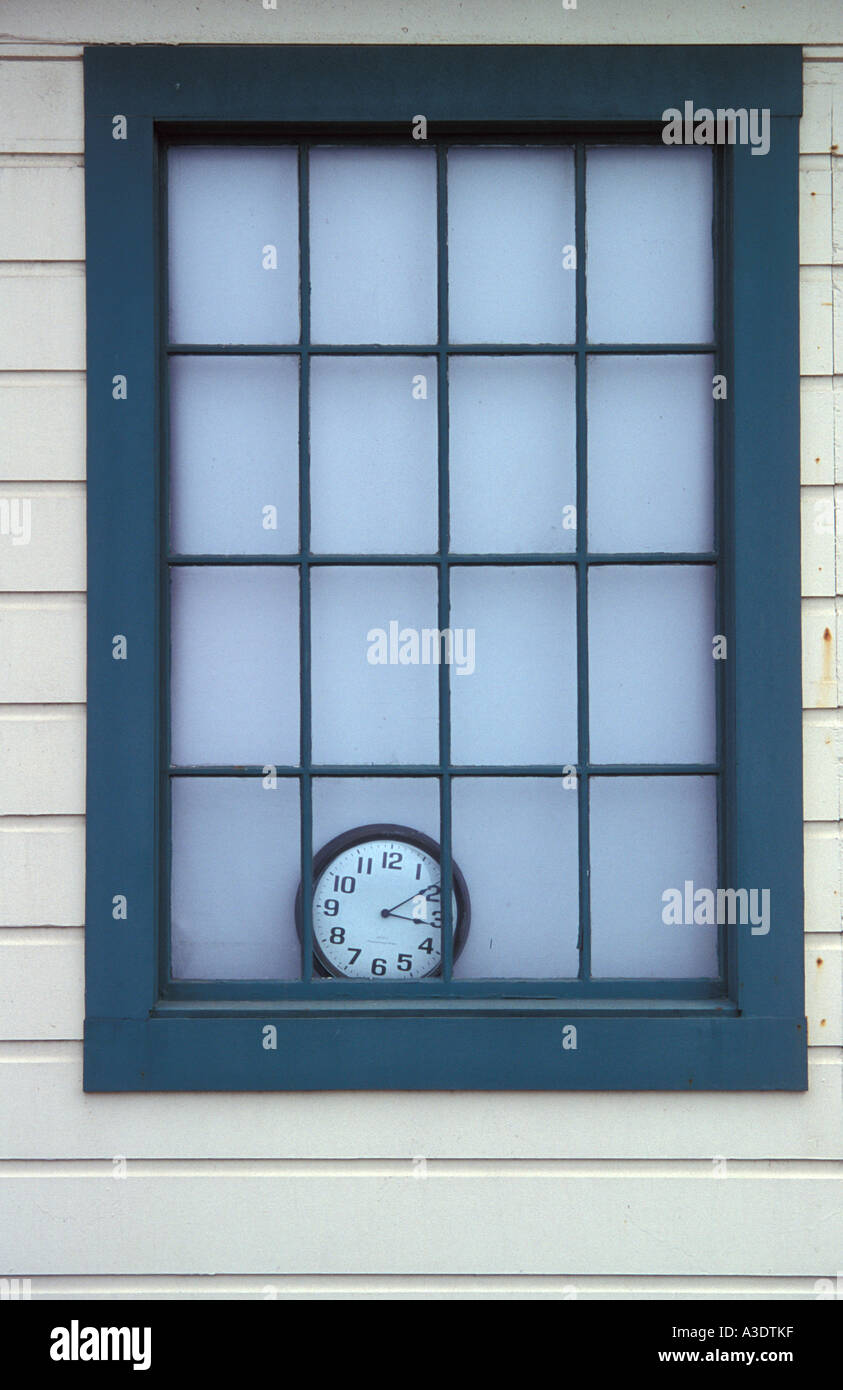 A clock sitting on windowsill of old wooden building, with white blind ...