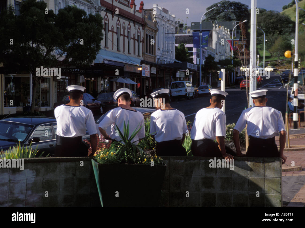 Five sailors in navy uniforms back-view sitting on a wall on a street ...