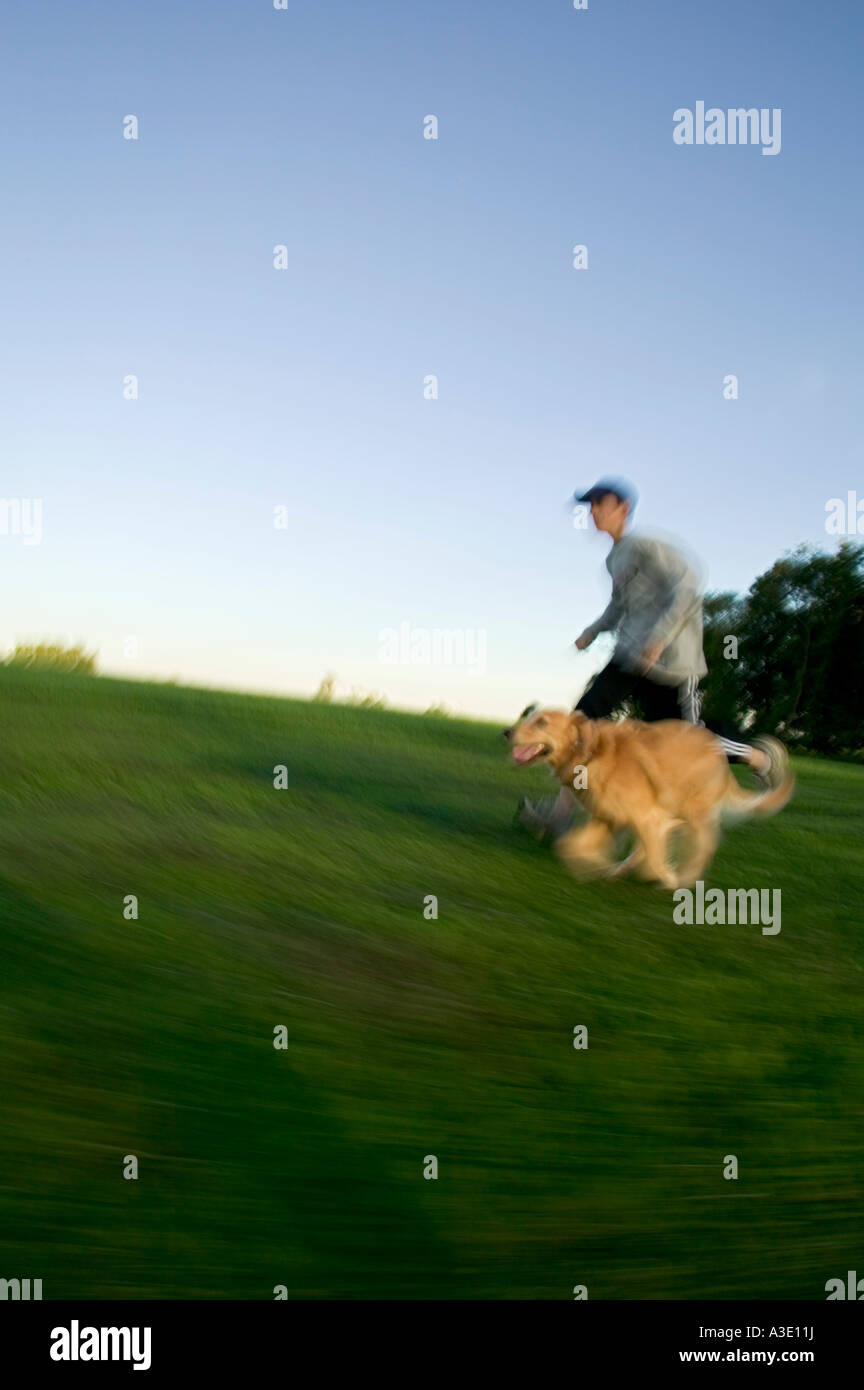 Teenage boy running with his Golden Retriever dog in the green grassy ...