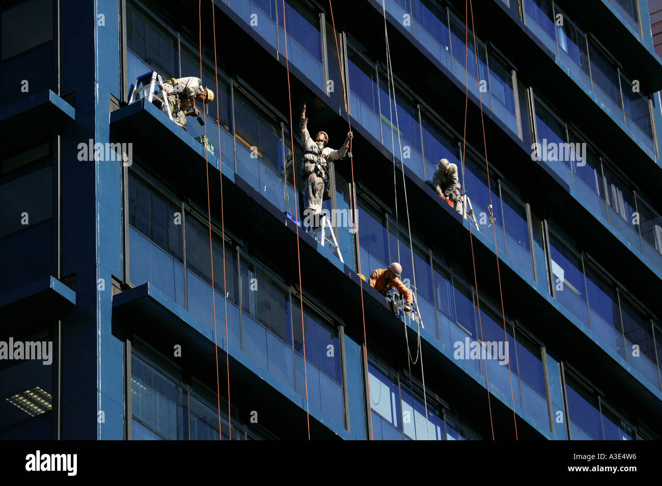 Men with hard hats and abseiling ropes painting ouside of multi-storey ...