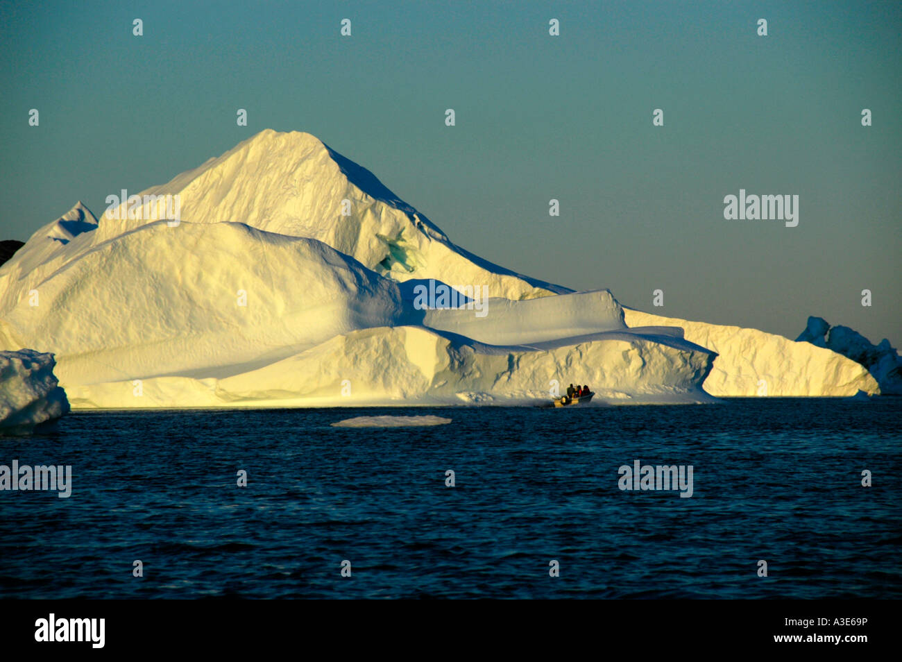Small motor boat at the edge of a huge iceberg Sermilik Fjord ...
