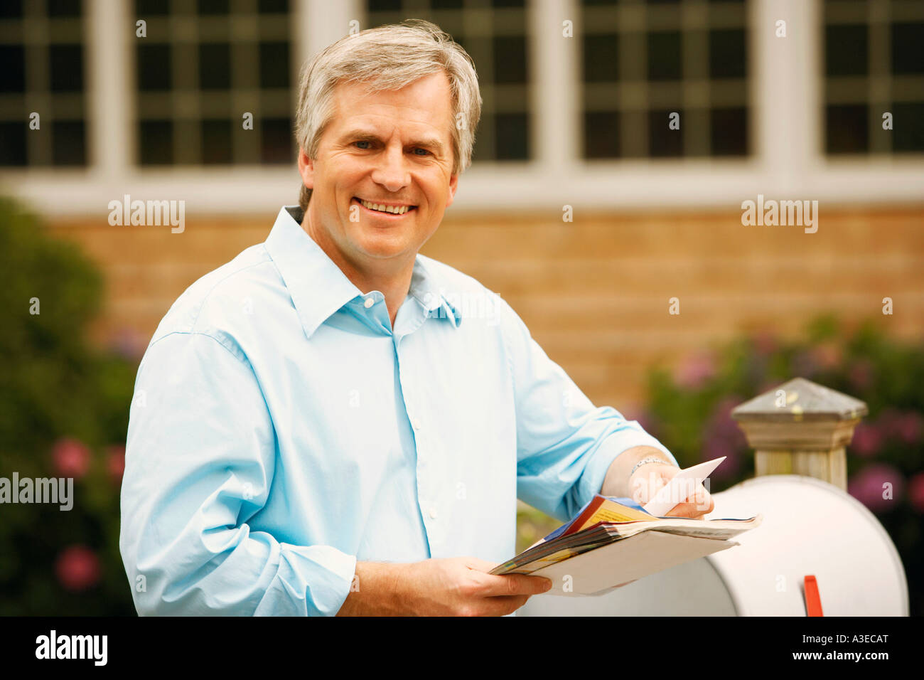 Portrait of a mature man standing by a mailbox and holding mails Stock ...