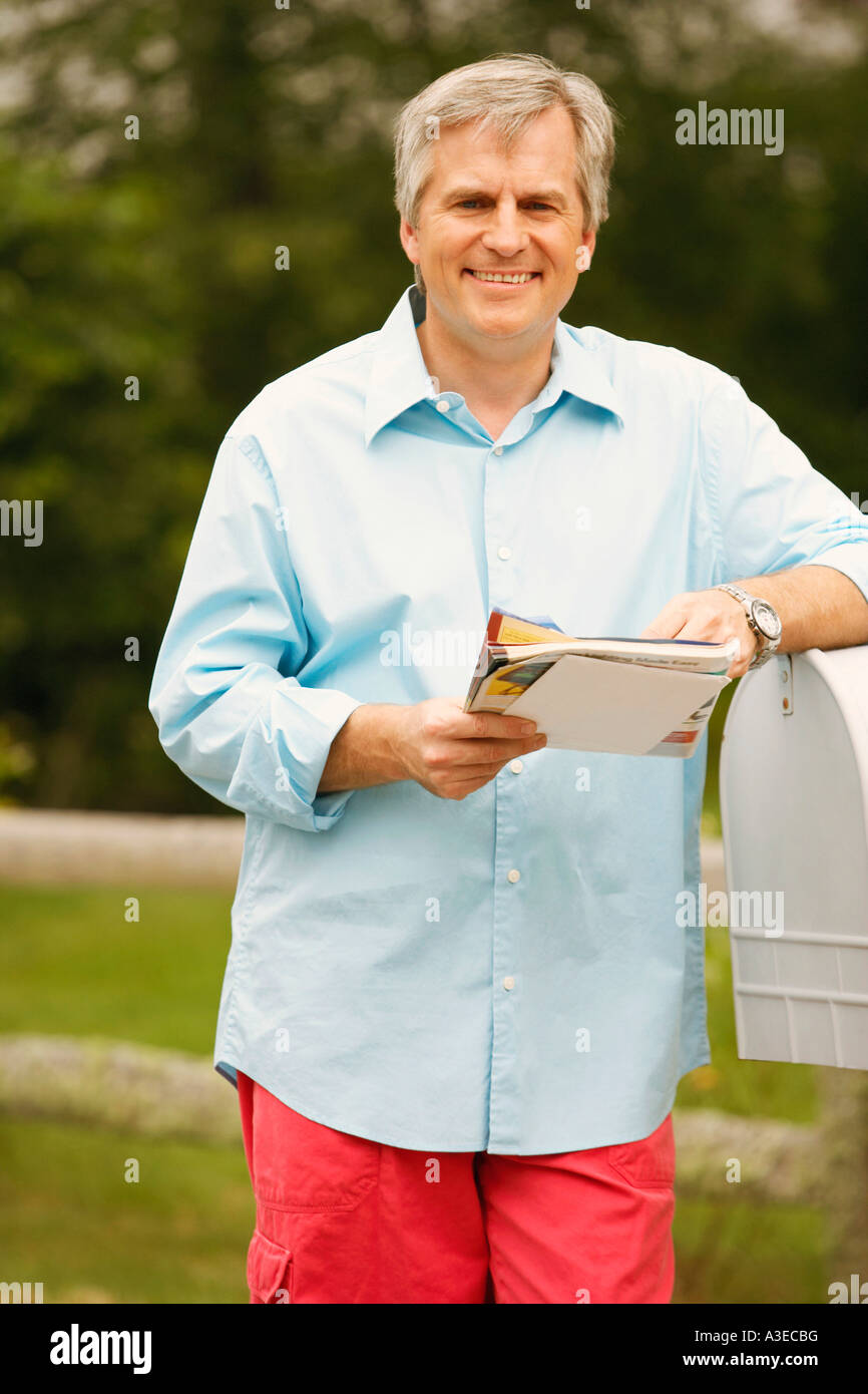 Portrait of a mature man standing near a mailbox and holding mails ...