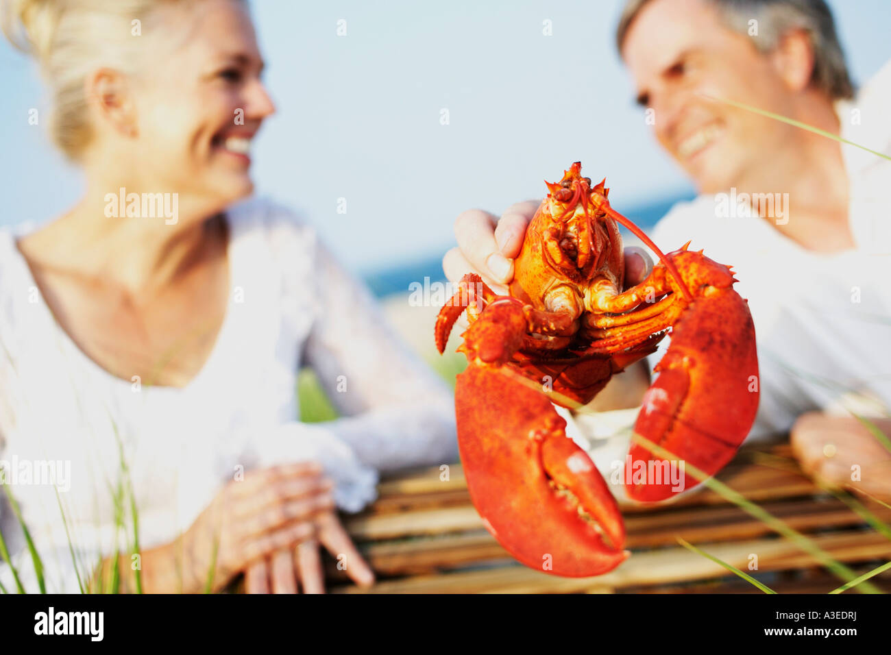 Close-up of a mature man holding a lobster with a mature woman sitting ...