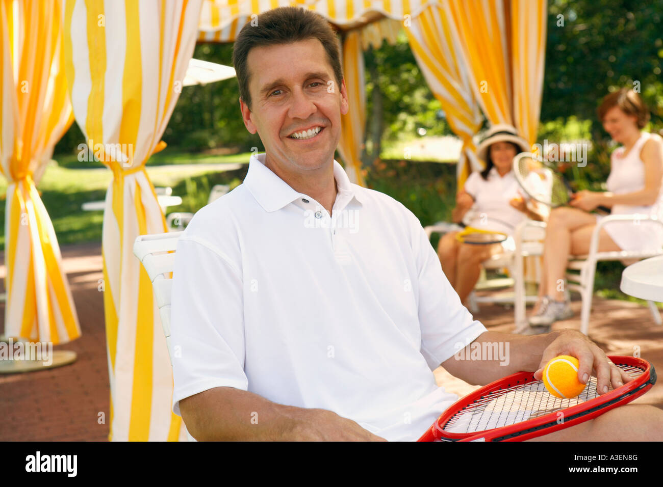 Portrait of a mature man sitting on a chair and holding a tennis ball ...