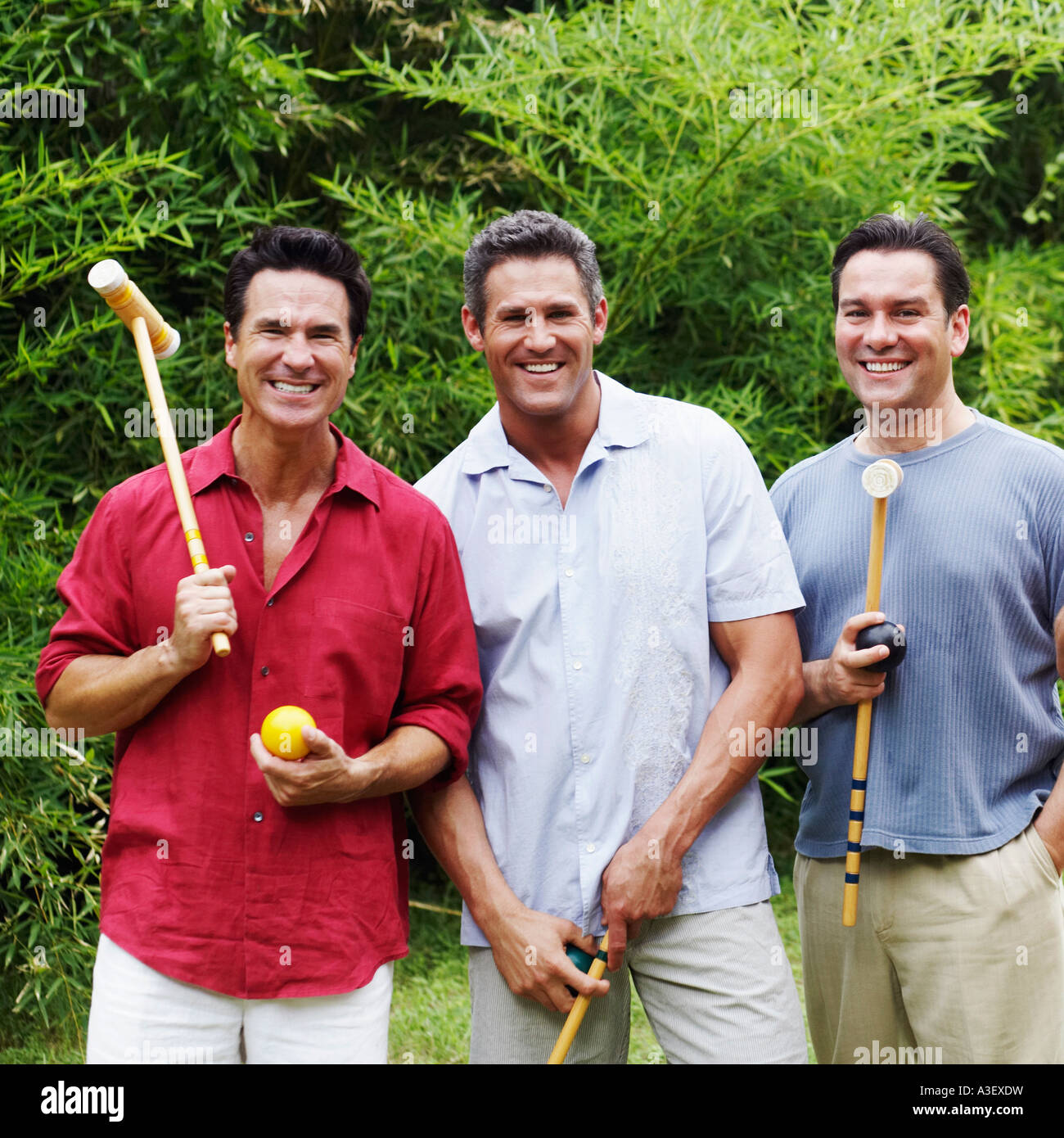 Portrait of a mid adult man with two mature men holding croquet mallets ...