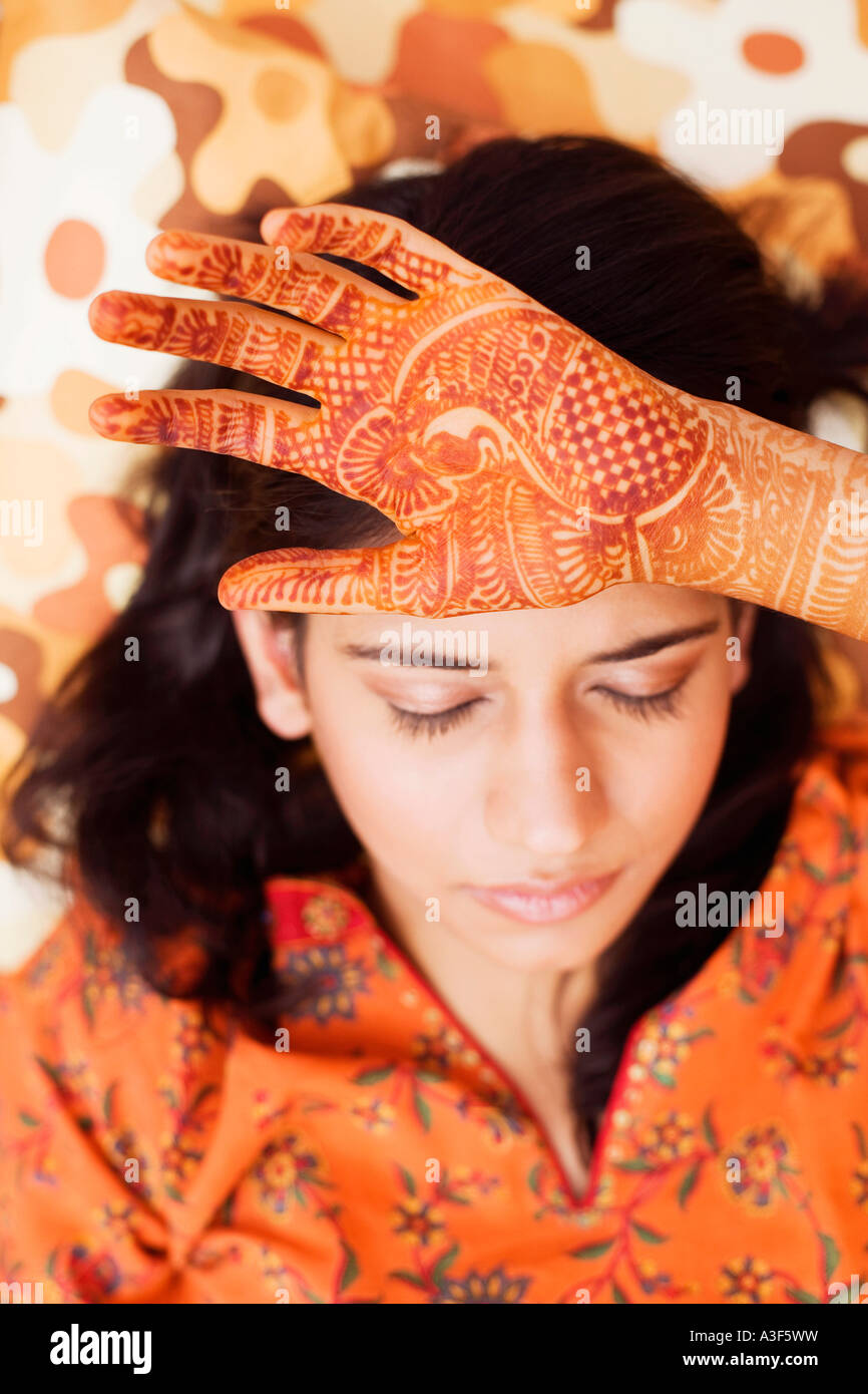 Close-up of a young woman with her henna tattooed hand on her forehead ...