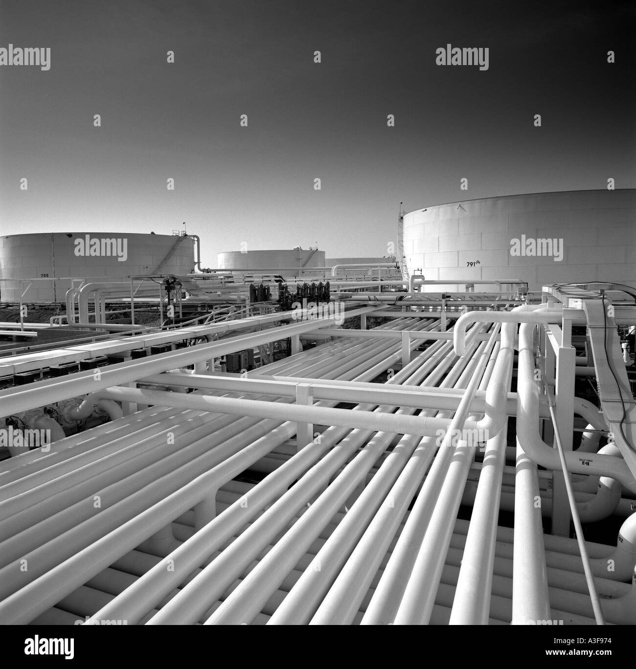 Row of pipes feed into refinery storage tanks Stock Photo - Alamy