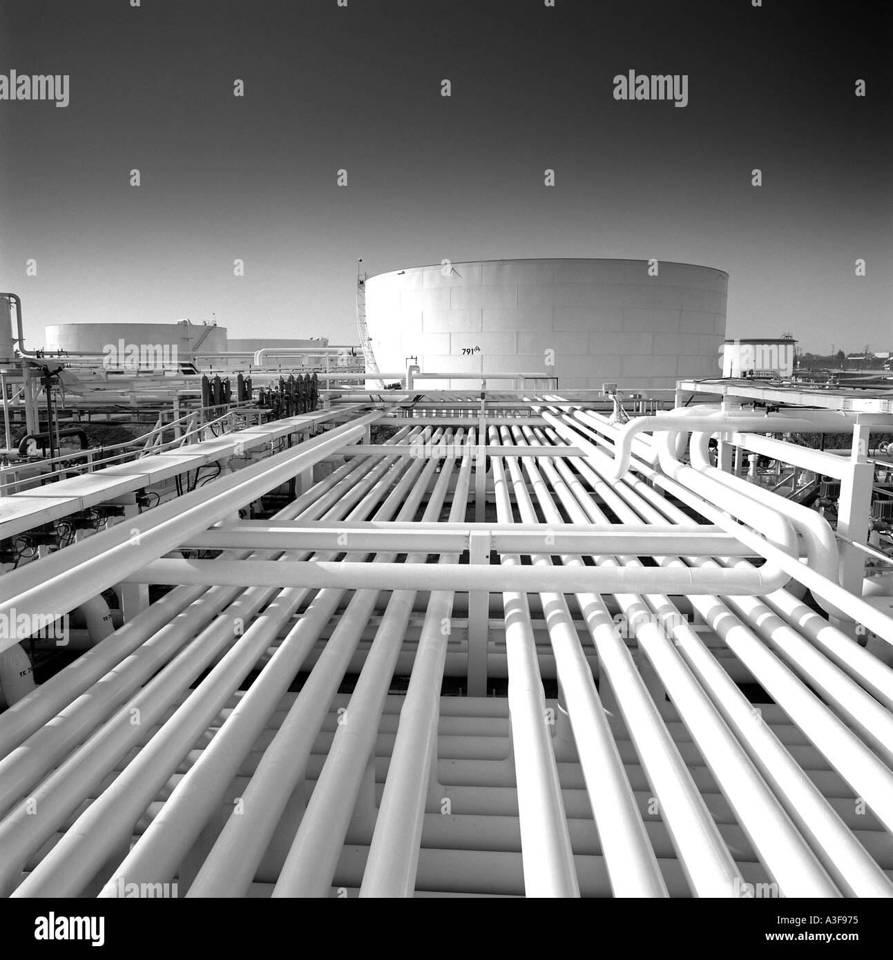 Row of pipes feed into refinery storage tanks Stock Photo - Alamy