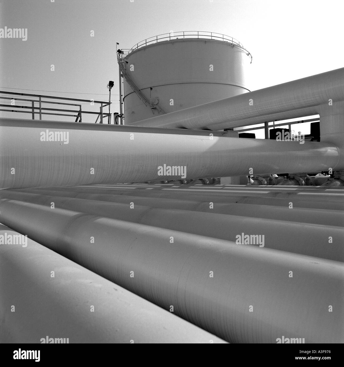Row of pipes feed into refinery storage tanks Stock Photo - Alamy