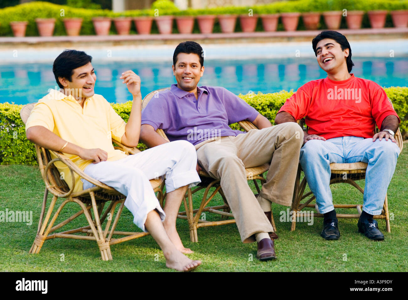 Three young men sitting on chairs at the poolside and smiling Stock ...