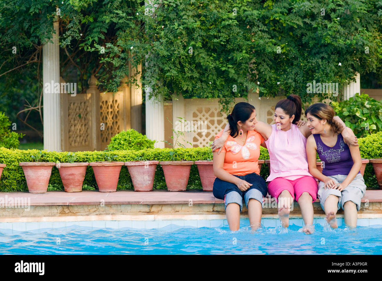 Three young women sitting at the poolside Stock Photo - Alamy