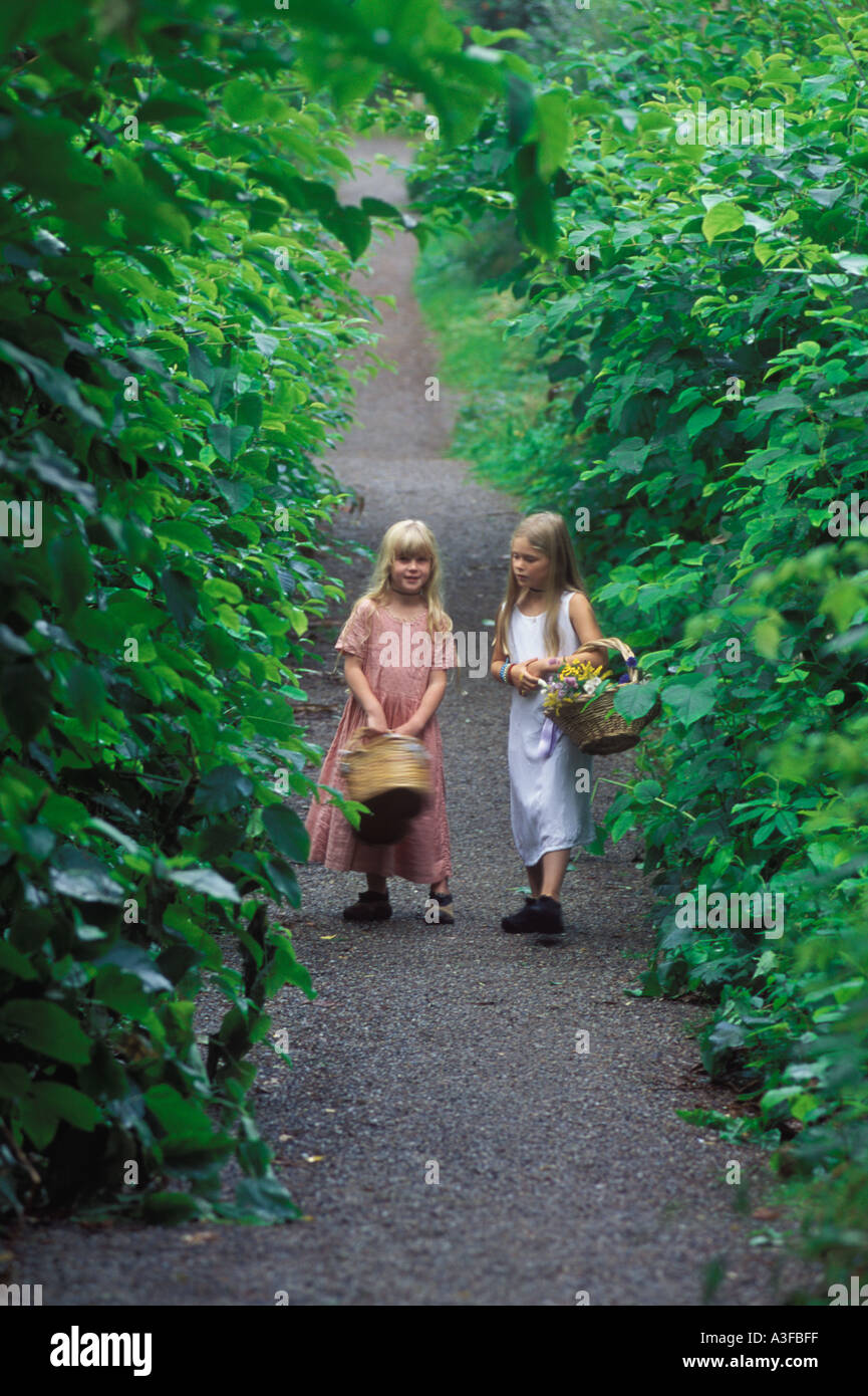 Two young girls on narrow pathway with summer dresses and baskets of ...