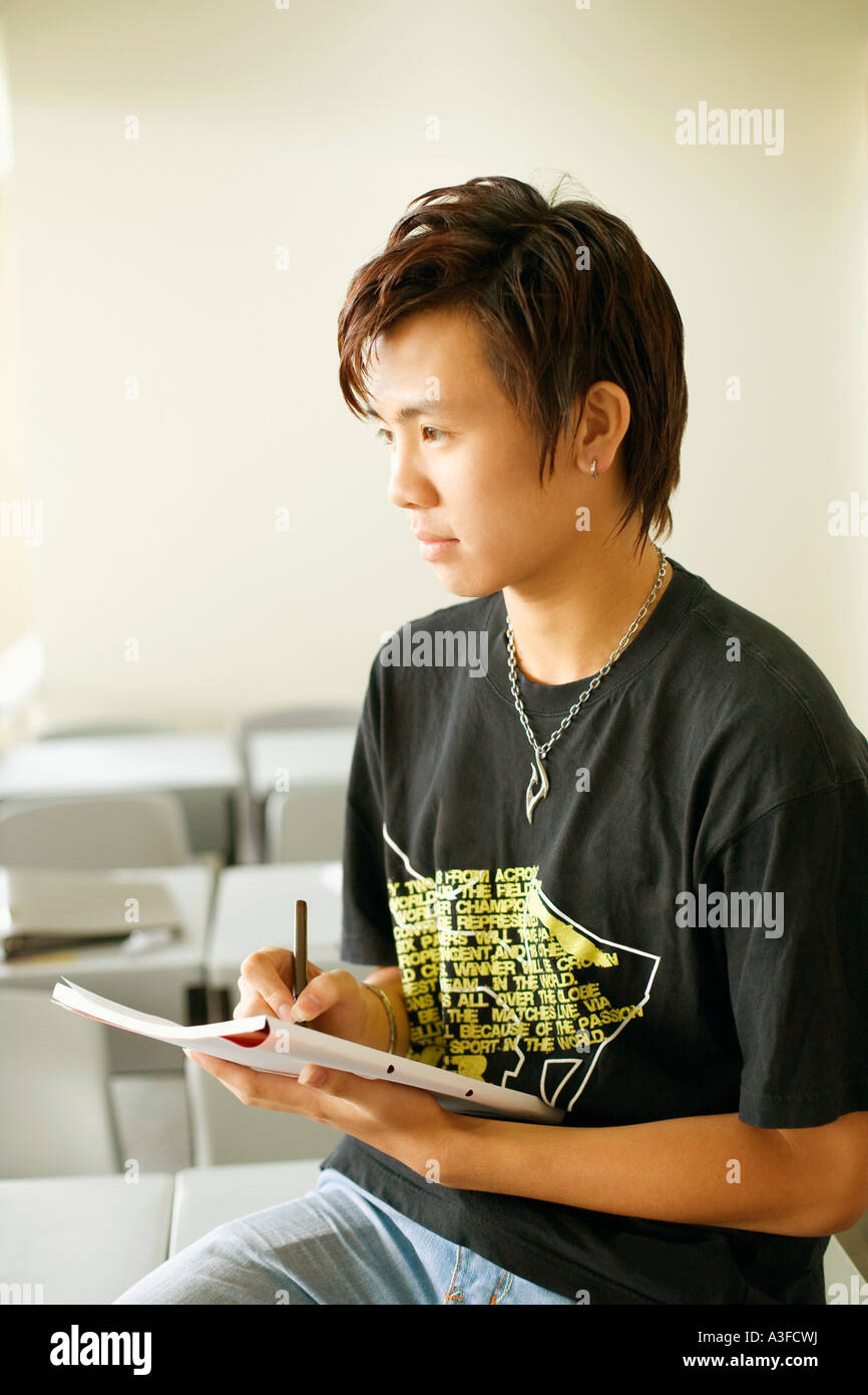 Close-up of a teenage boy writing on a notepad and sitting in the ...