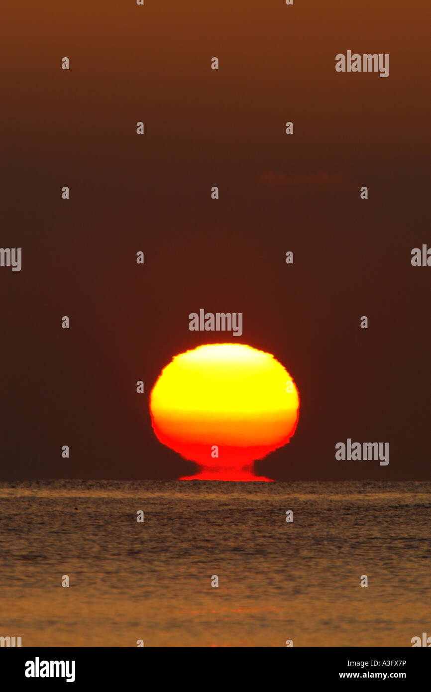 sun rising over sea coloured yellow white and red distorted by ...