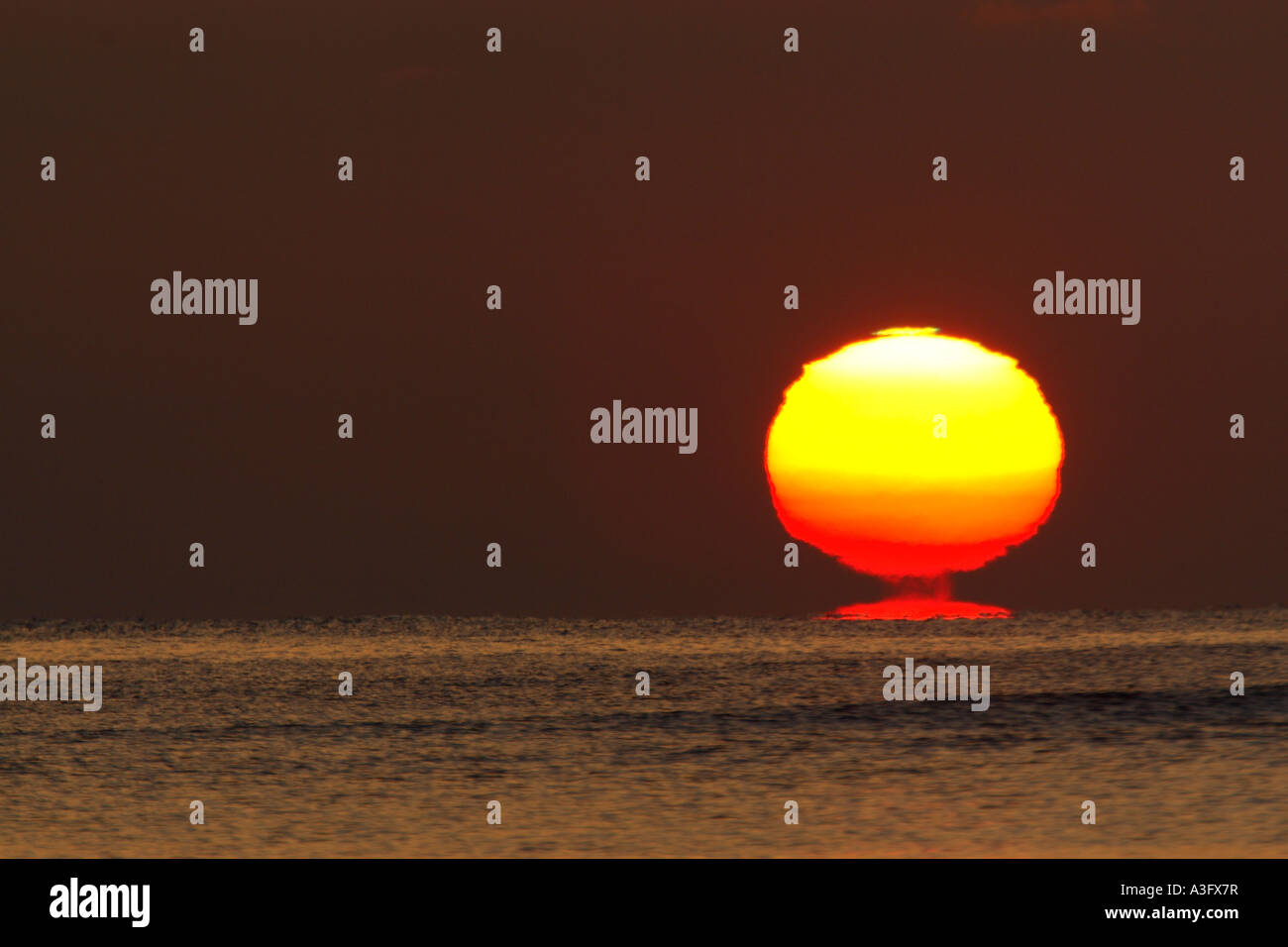 sun rising over sea coloured yellow white and red distorted by ...
