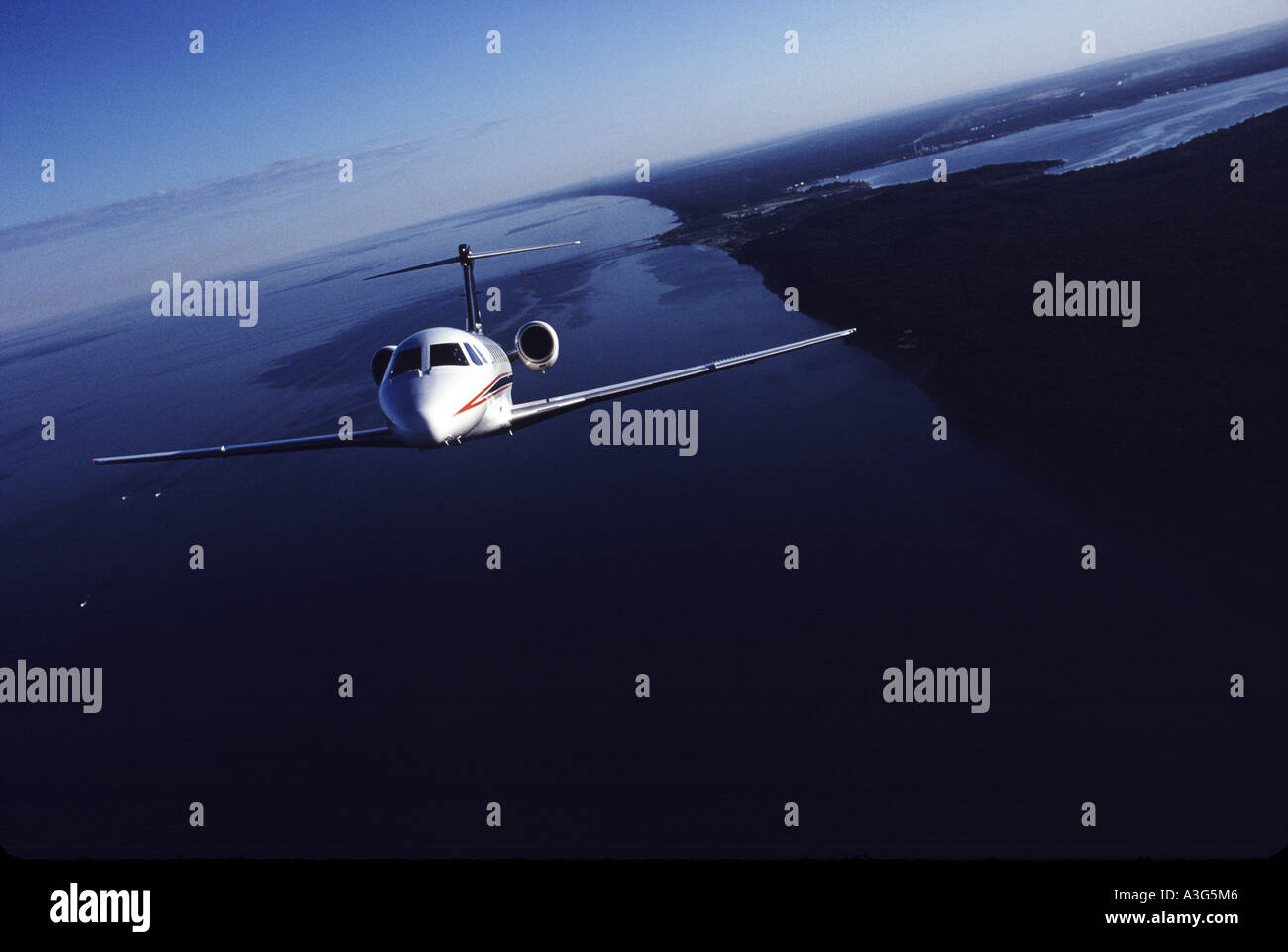 Front overhead view of a white private airplane flying over land and ...