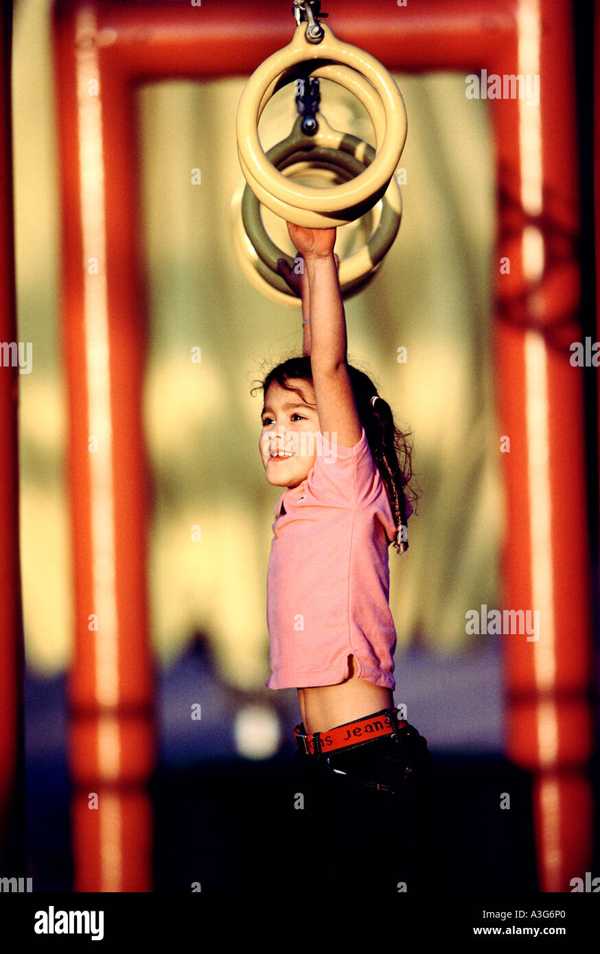 Portrait of an adorable young kid hanging on playground rings smiling ...
