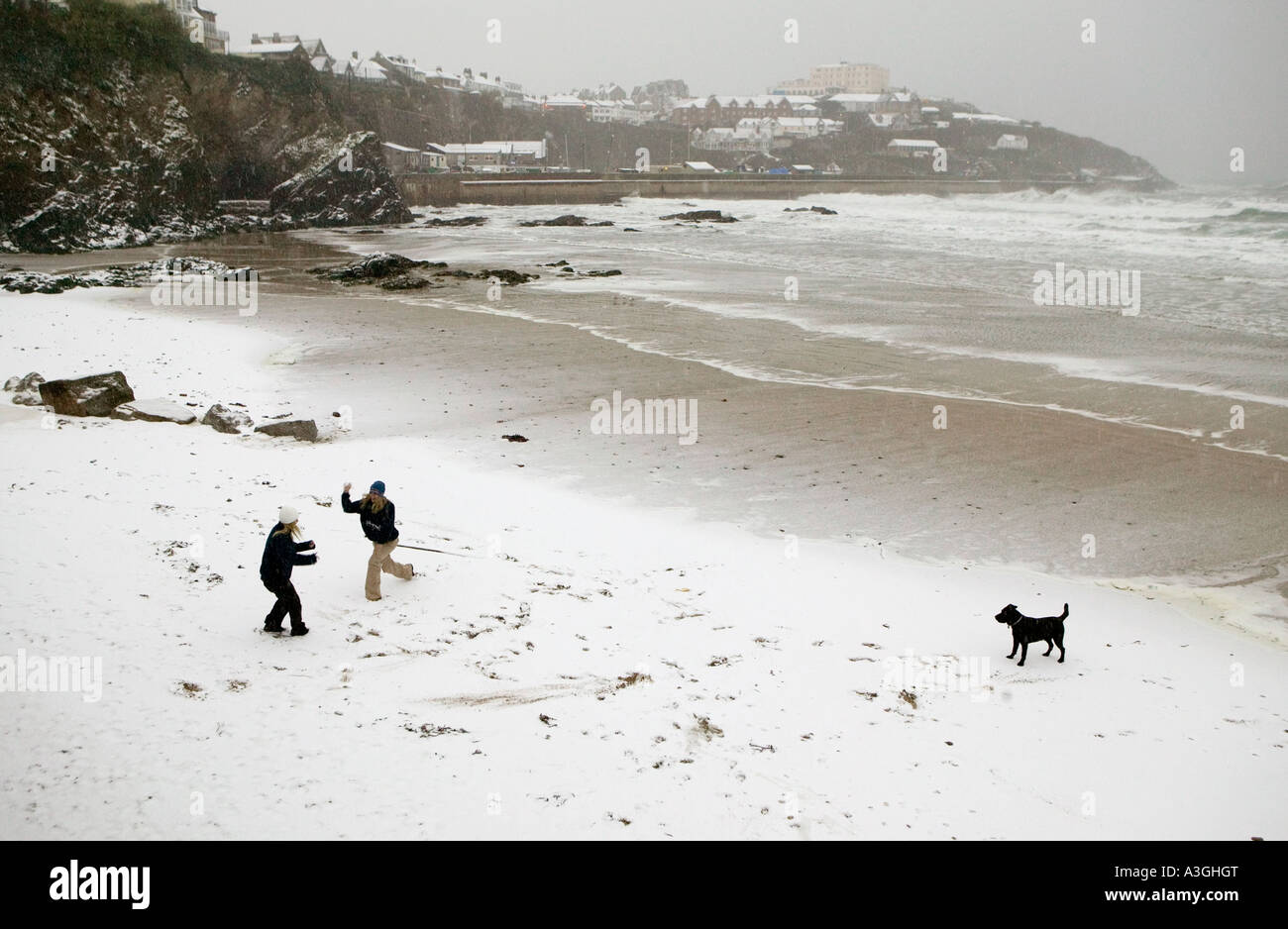 Two young women play with a black labrador on a snow covered Towan ...