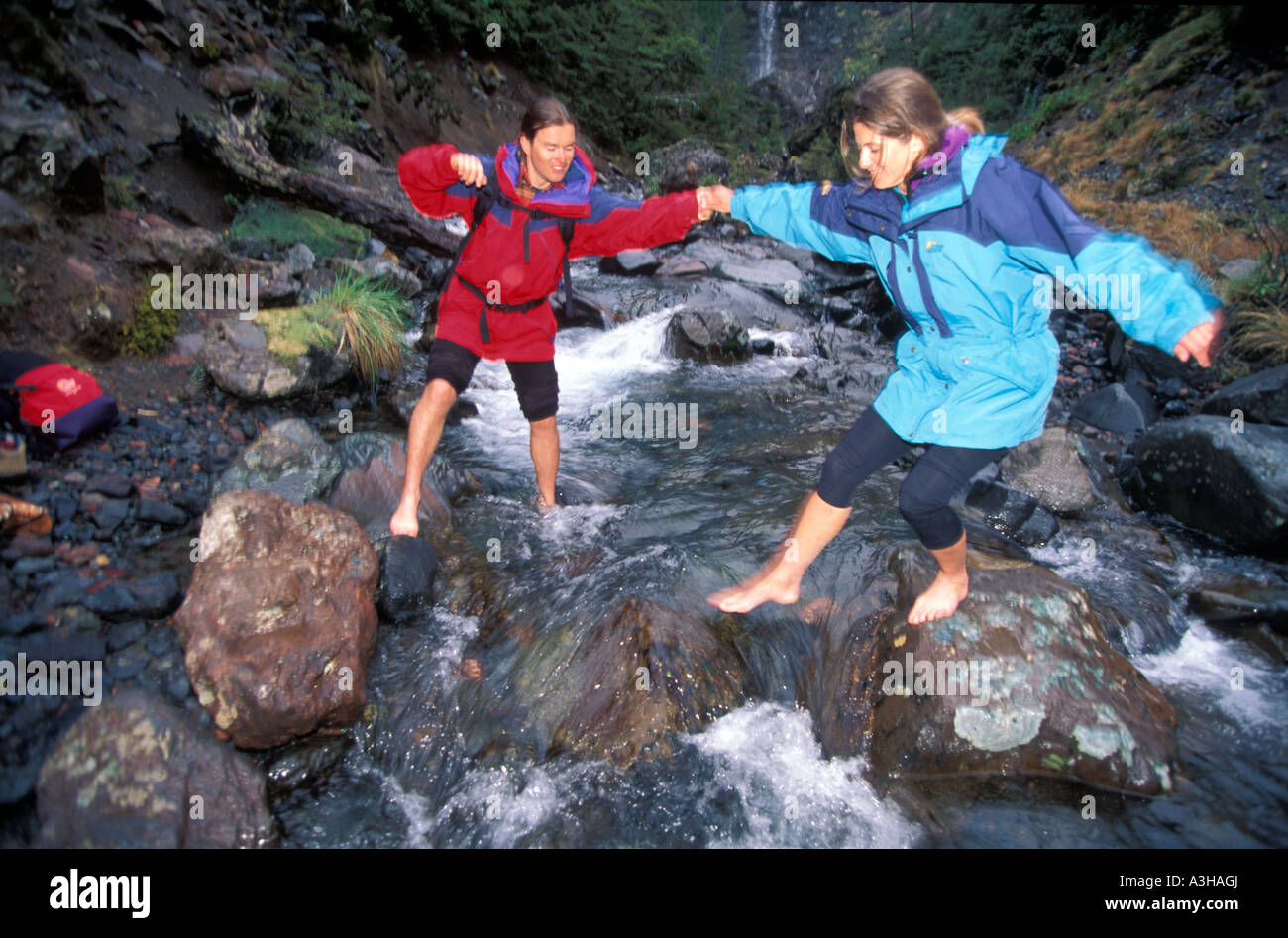 Couple helping each other cross a river Stock Photo - Alamy