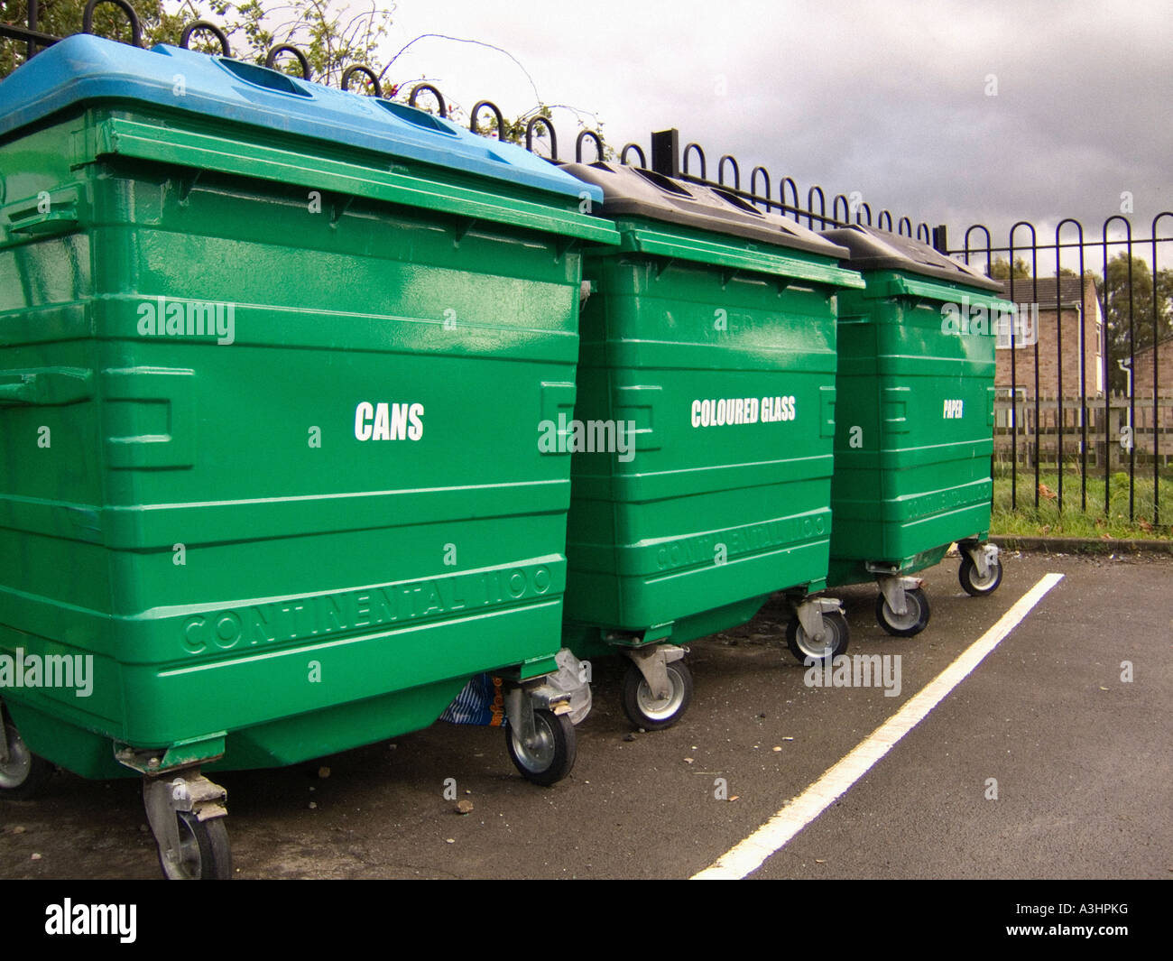 Three green-coloured industrial-sized recycling bins in a car park, one ...