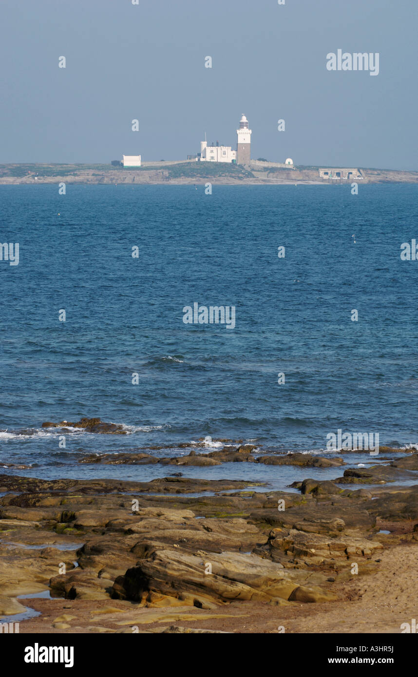 Deserted rocky beach at Amble with Coquet island lighthouse sitting on ...