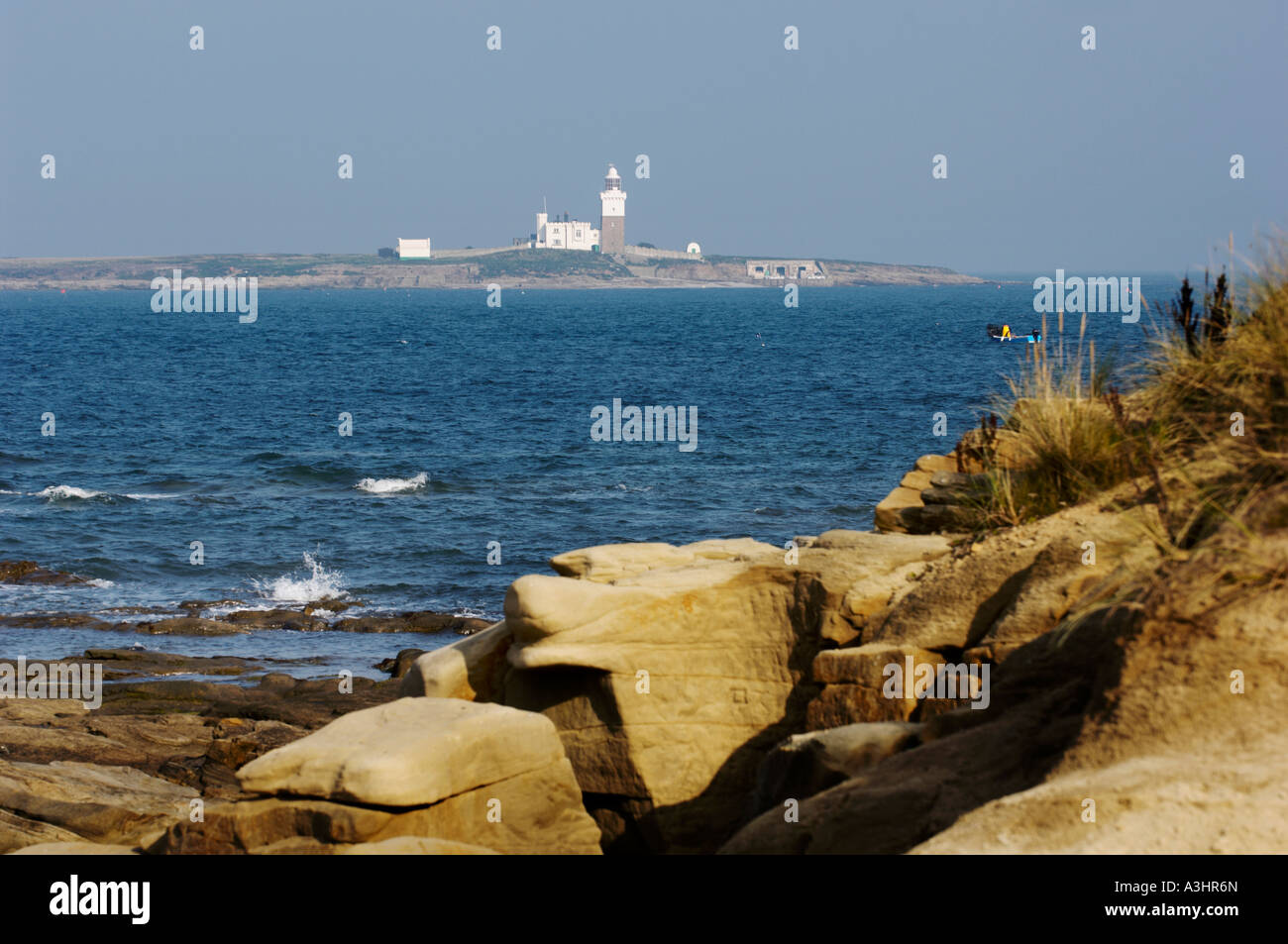 Deserted rocky beach at Amble with Coquet island lighthouse sitting on ...