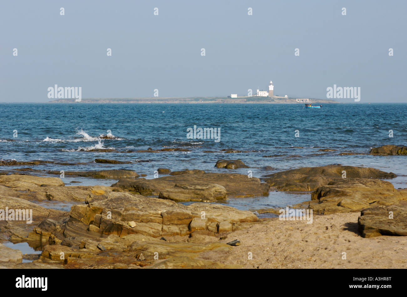 Deserted rocky beach at Amble with Coquet island lighthouse sitting on ...