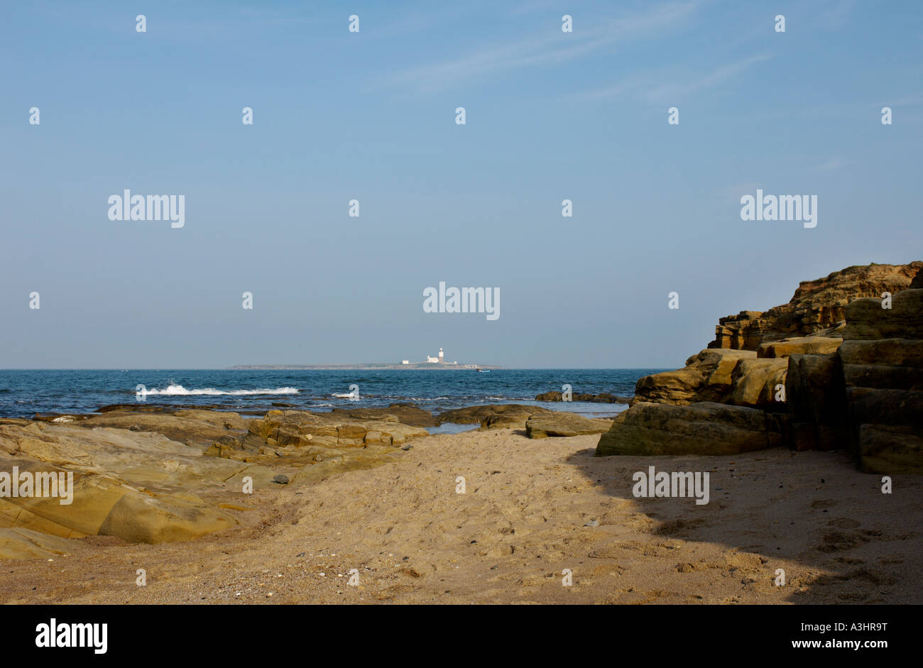 Deserted rocky beach at Amble with Coquet island lighthouse sitting on ...
