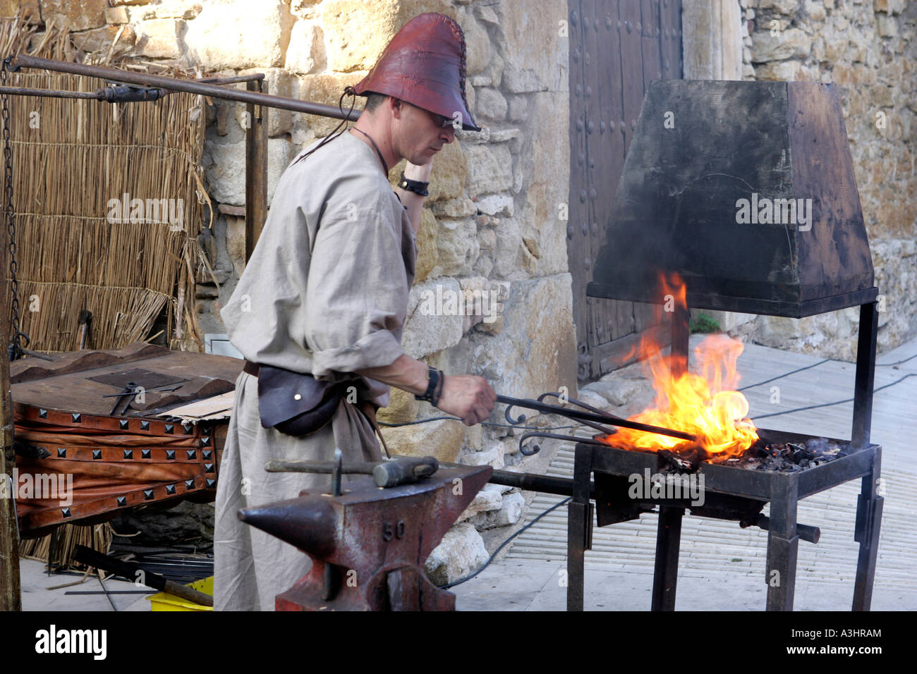 Blacksmith in medieval costume forging steel with fire in village of ...