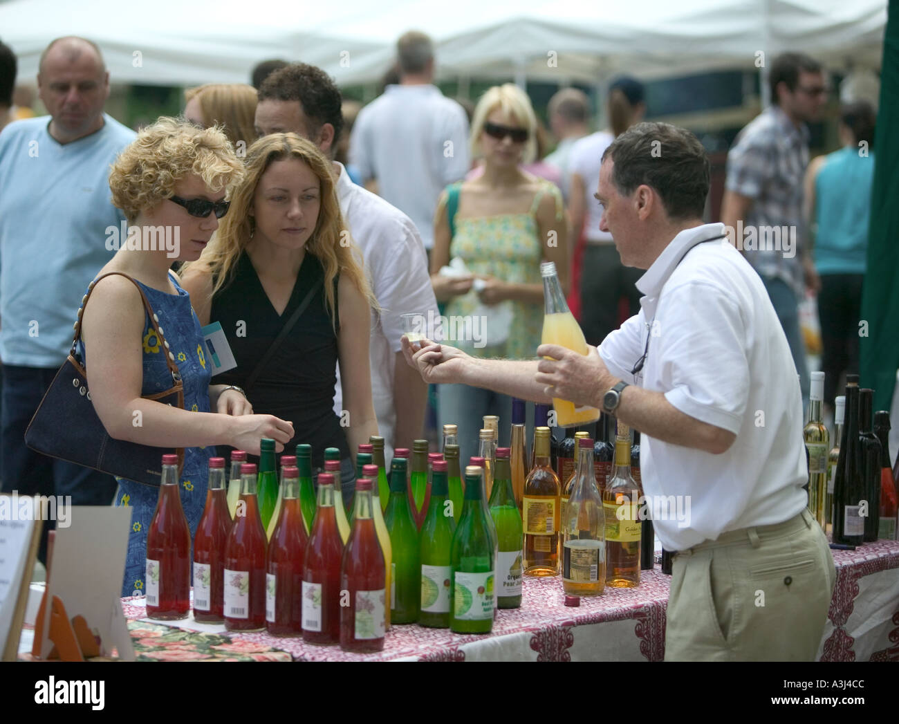 Man offering two women samples of organic wine cider and pear juice at ...