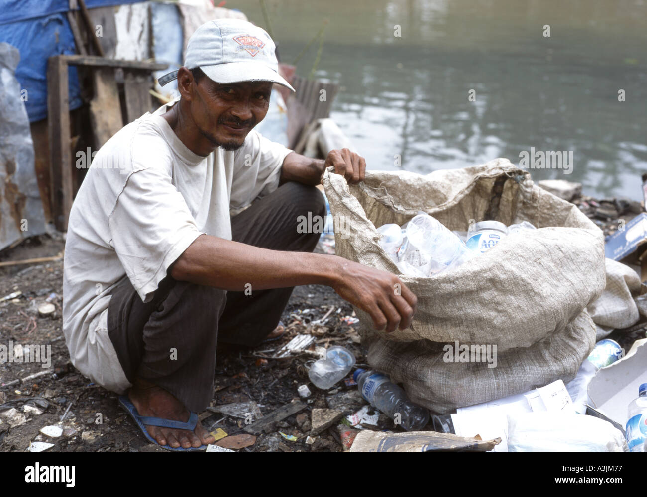 Smiling local man collecting empty plastic bottles by the river in a ...