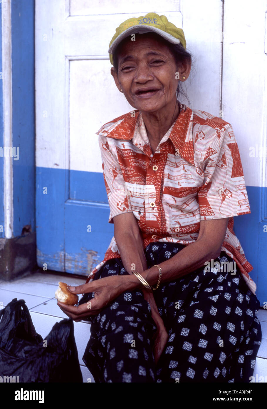 Smiling toothless homeless woman eating a small cake at the roadside in ...