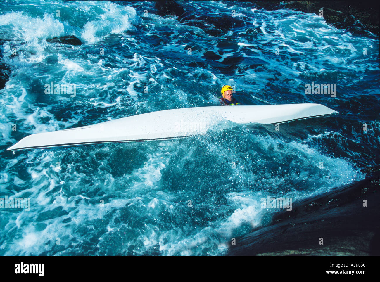 A sea kayak paddler capsized in turbulent breaking sea next to rocky ...