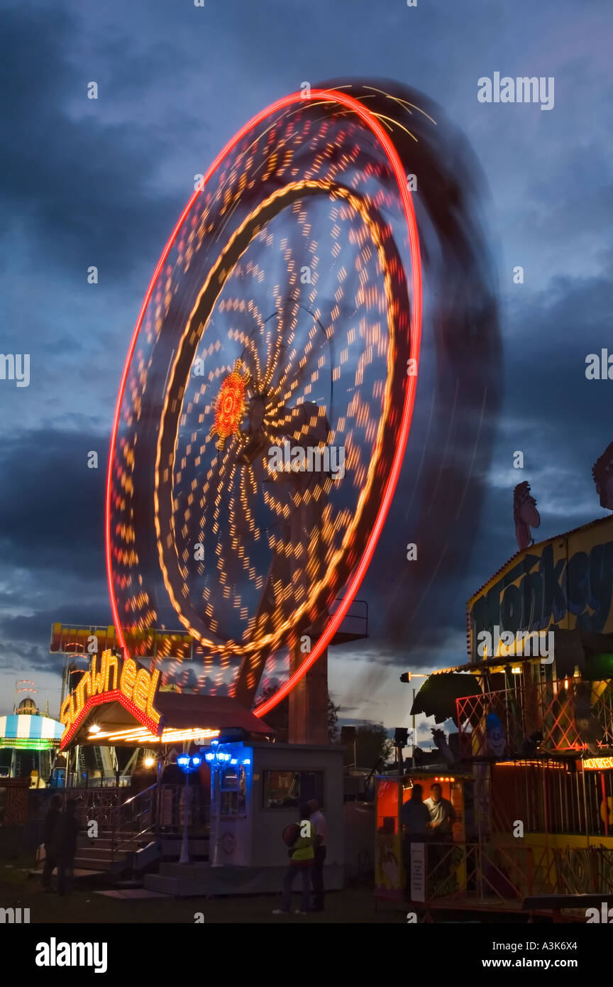 A ferris wheel at a fairground, spinning at night. The Big Cheese ...