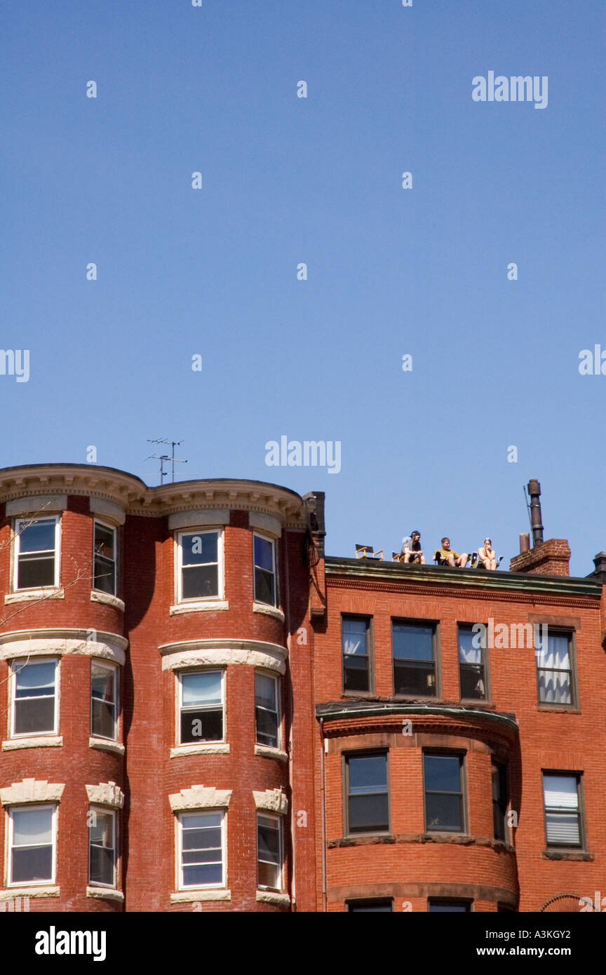 Young people watch the Boston Marathon from the roof of a red brick ...