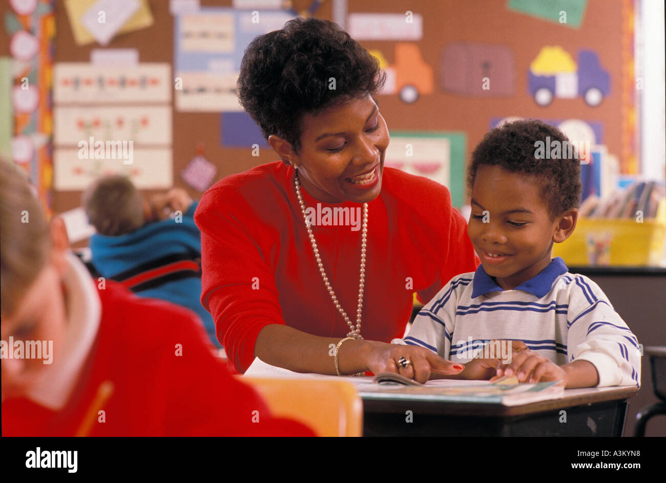 African American teacher assisting male student in elementary classroom ...
