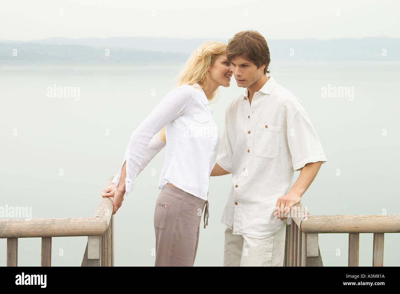 MR Flirting lovers leaning against a wooden railing in front of a lake ...