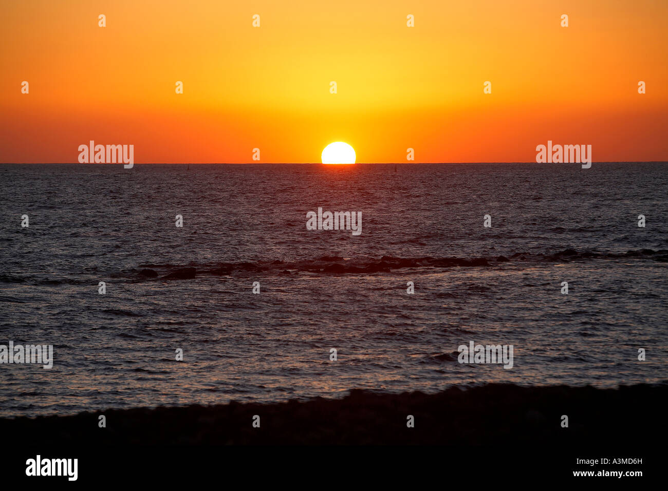 Bright orange sunset with the sun touching the Horizon line looking ...