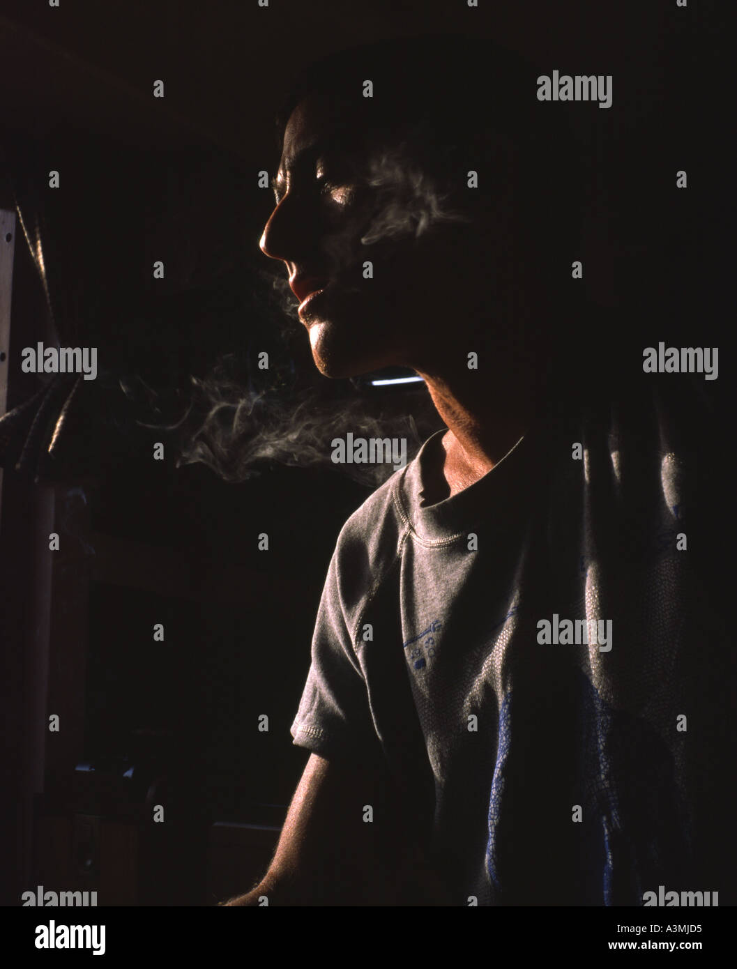 A man smokes a cigarrette in a shaft of light coming through a small ...